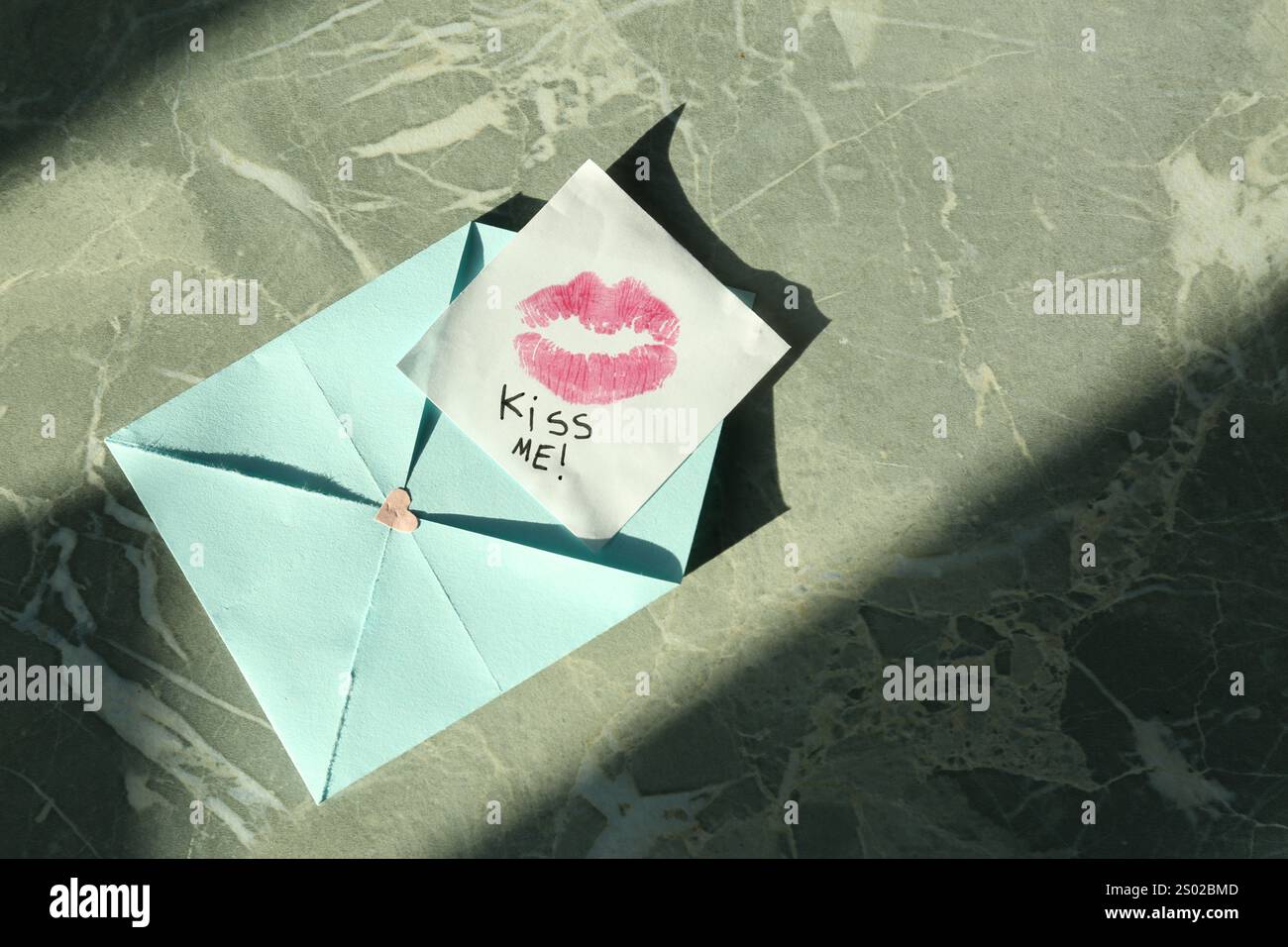 Note with phrase Kiss Me, lipstick mark and envelope on grey marble ...