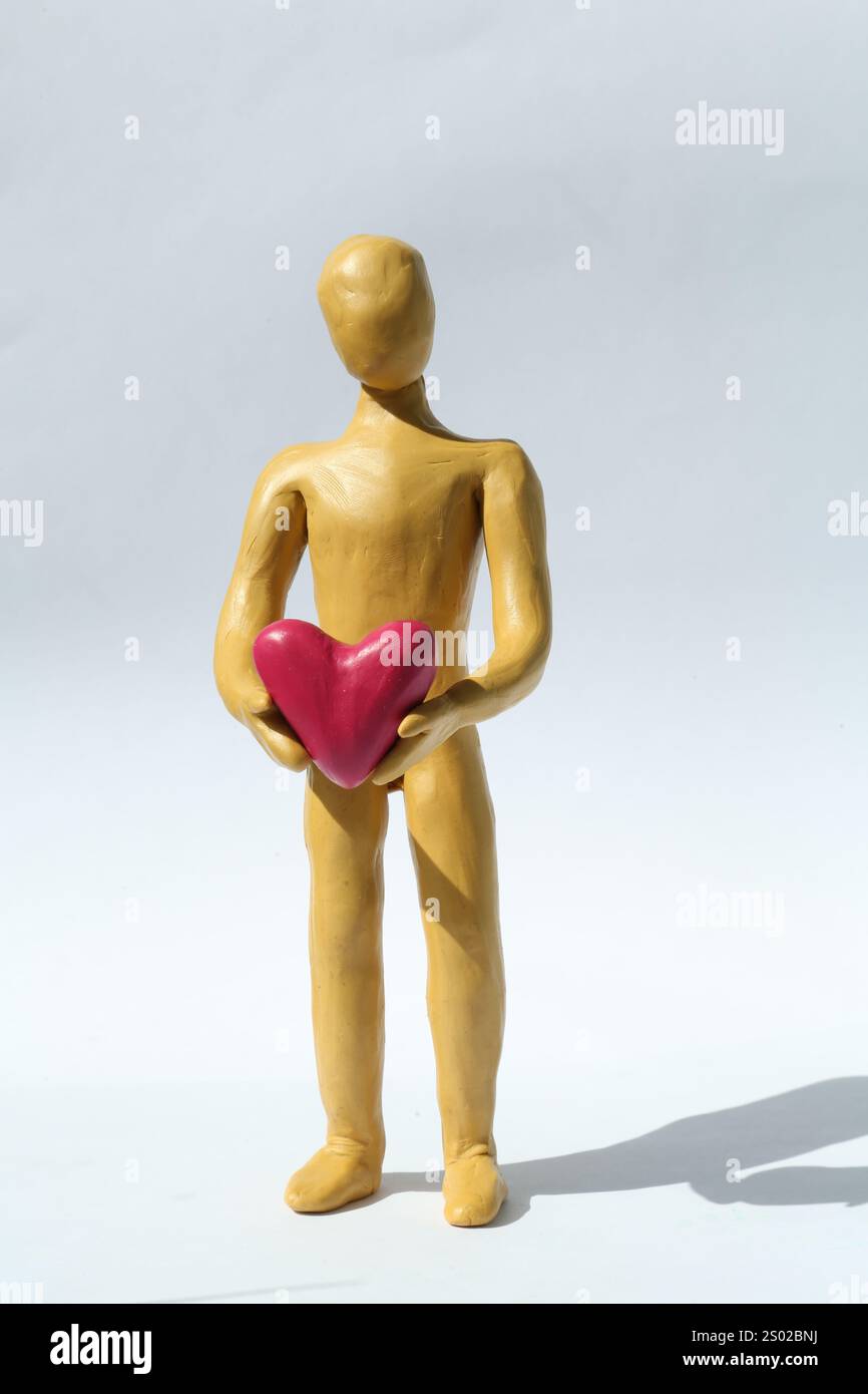 Yellow plasticine human figure with pink heart on white background ...