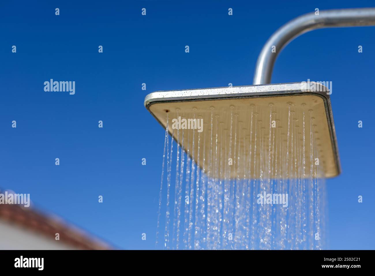 Square outdoor shower head with water flowing, captured against a clear ...