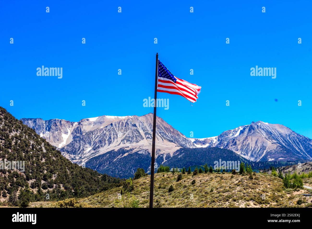 A flag is flying high in the sky above a mountain range. The flag is ...