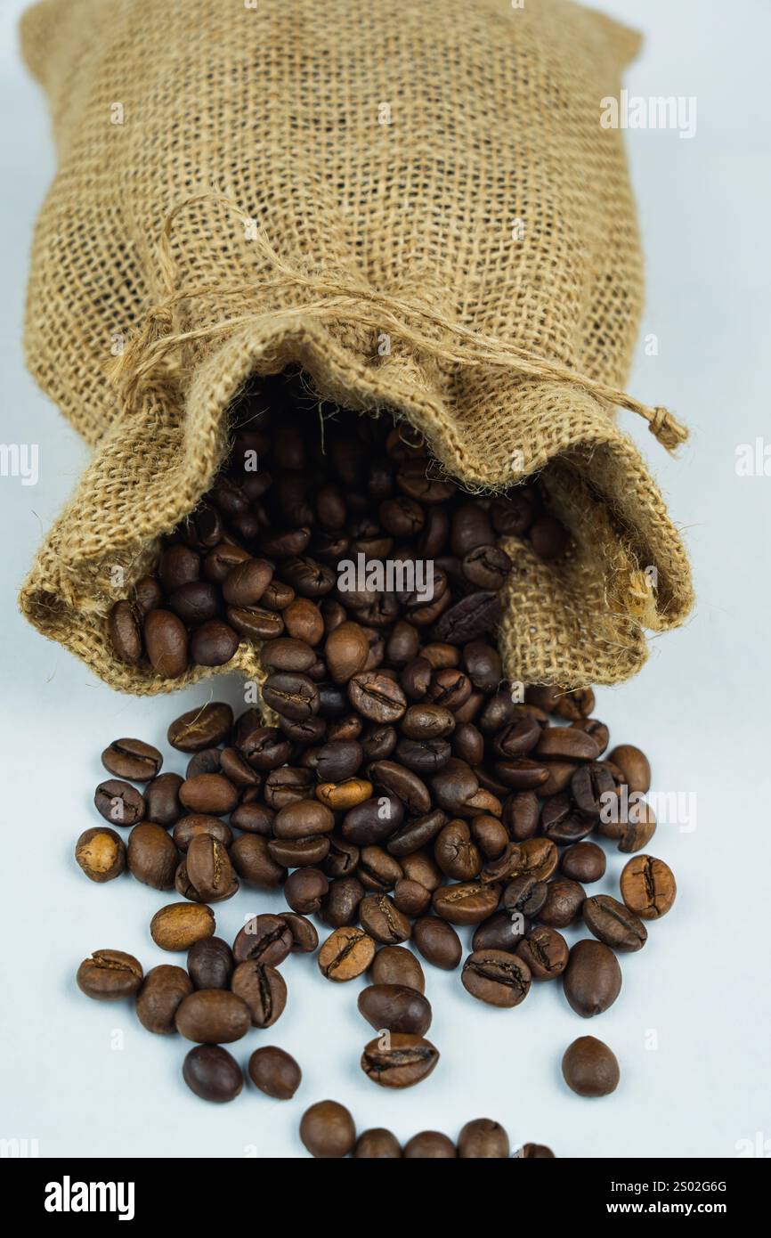 Burlap sack filled with roasted coffee beans spilling onto a white background, highlighting the ...