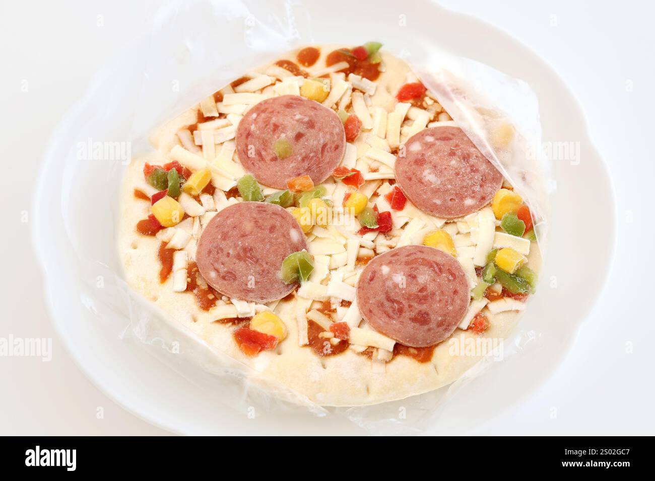 Frozen pizza in open plastic foil ready to thaw on plate, on white ...