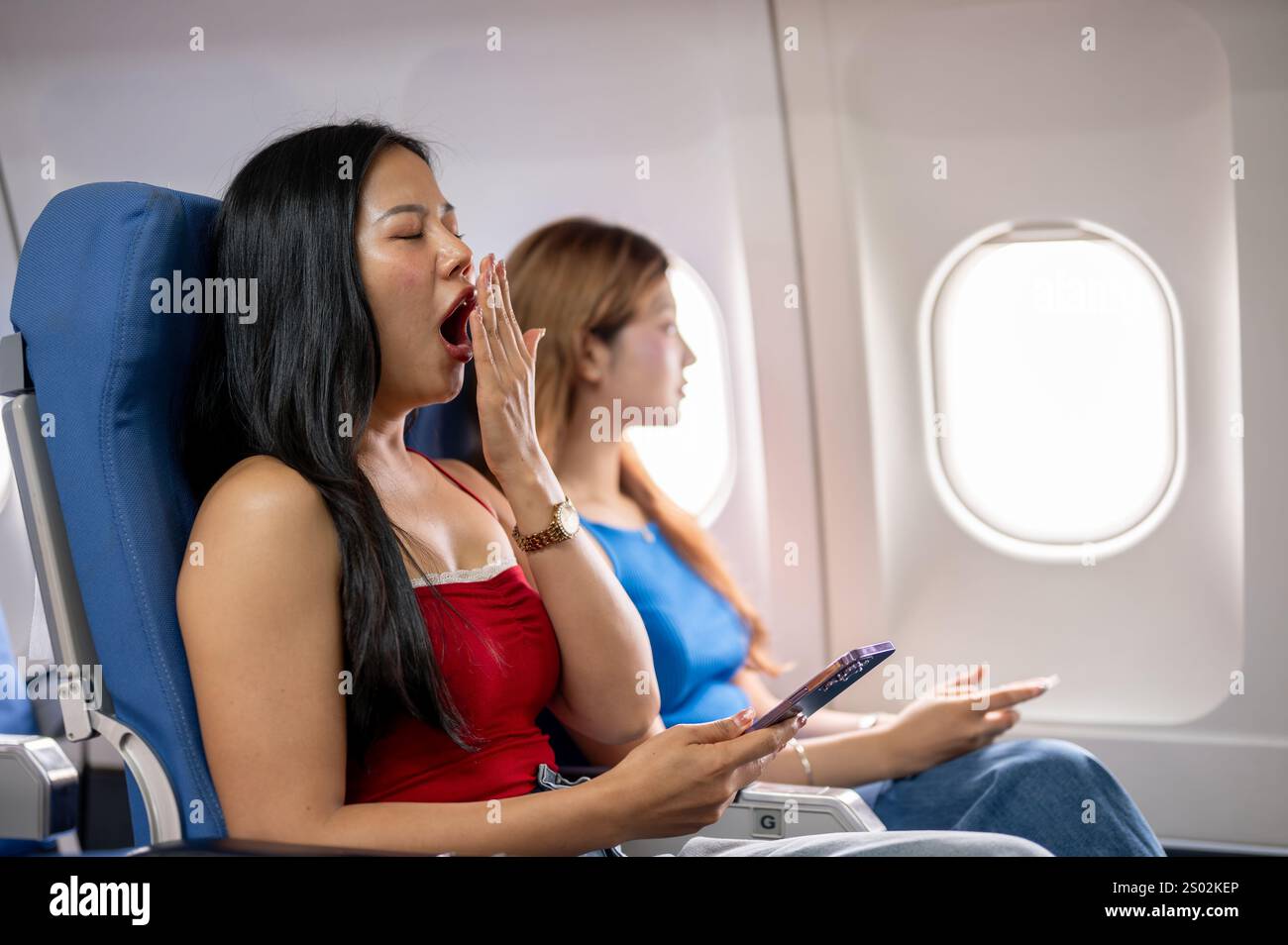 A tired, sleepy Asian female passenger covers her mouth while yawning, feeling sleepy during the ...