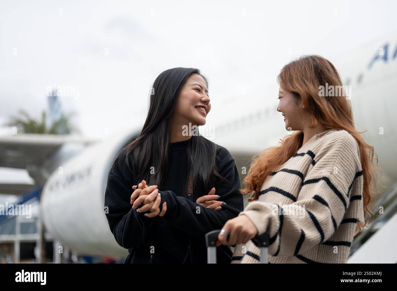 Two cheerful Asian female passengers with their luggage are standing ...