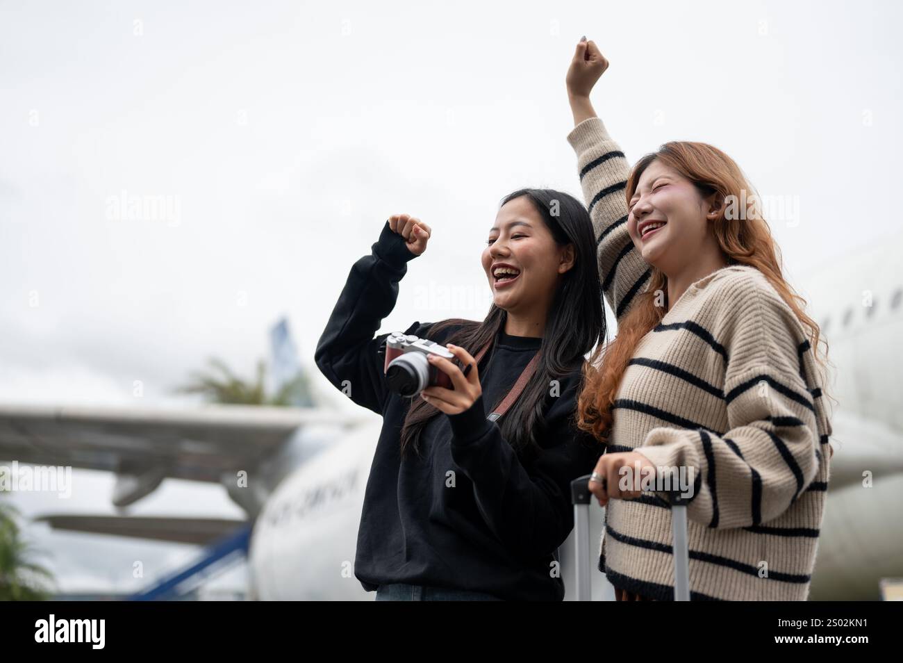 Two cheerful Asian female passengers with their luggage are standing ...