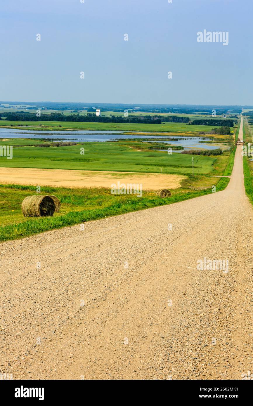 A long road with a field of hay and a body of water in the background ...