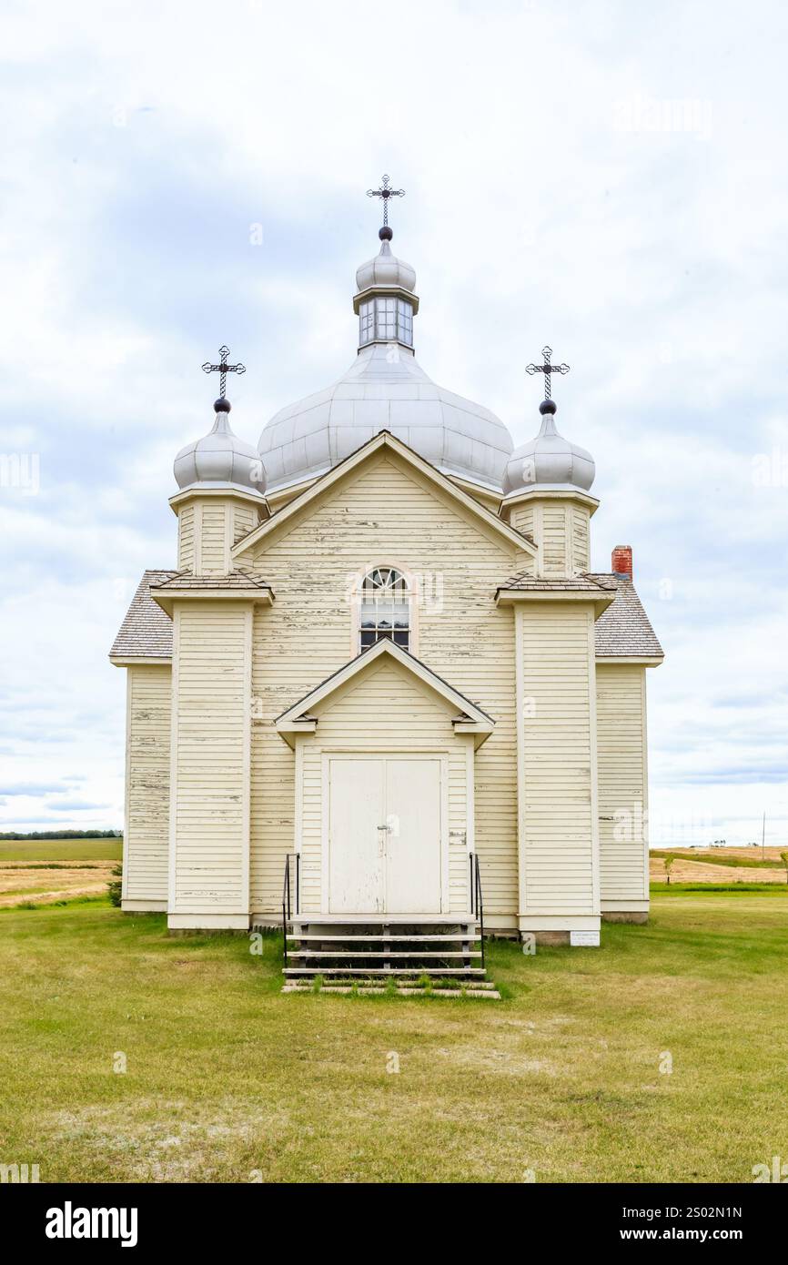 A small white church with a steeple and a cross on top. The building is ...
