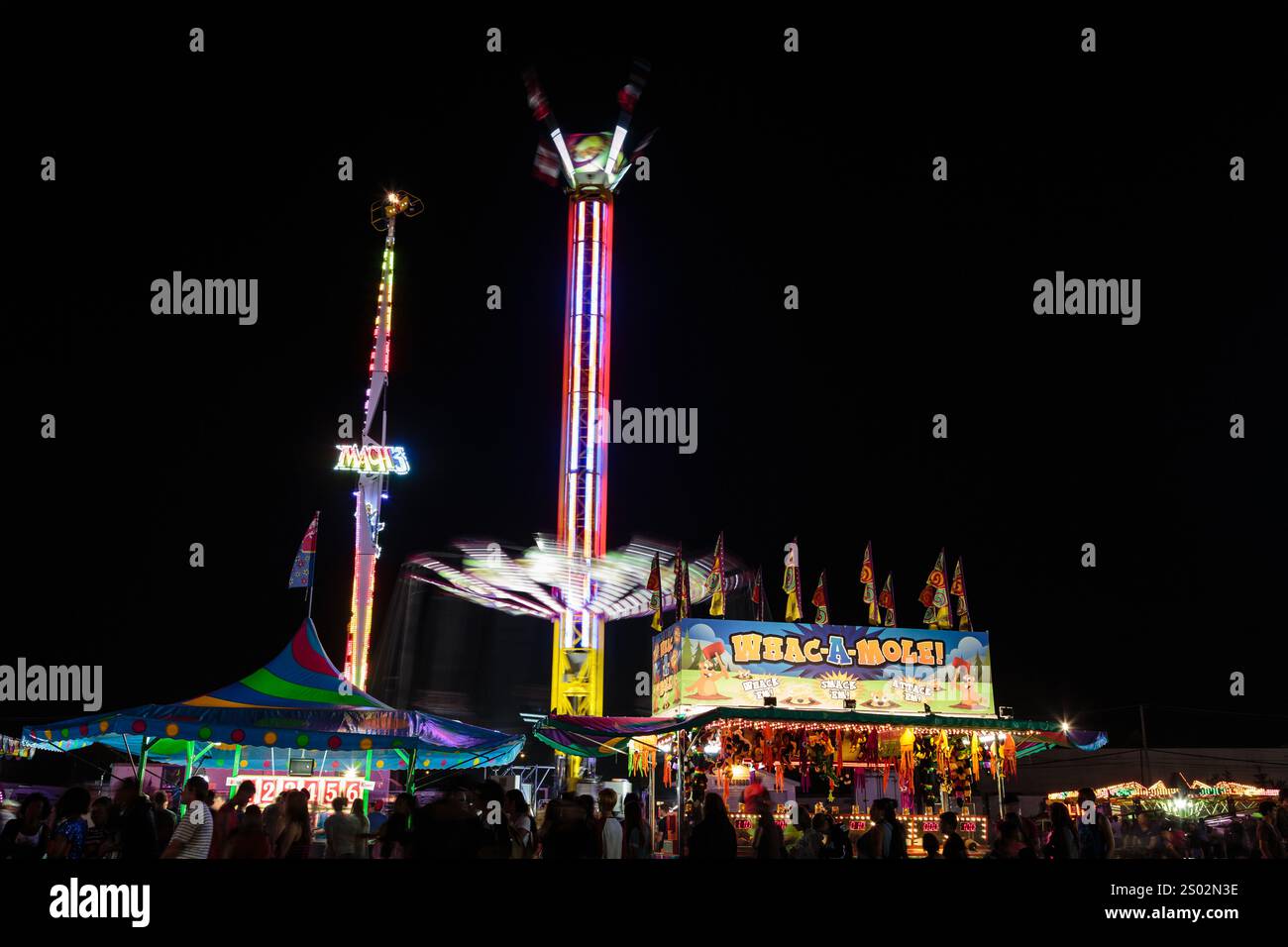 A carnival with a lot of people and a tall ride. The carnival is lit up ...
