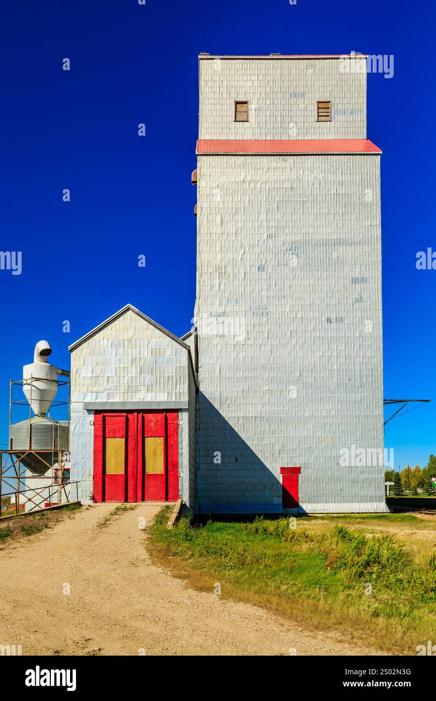 A large grain silo with red doors sits in a field. The silo is ...