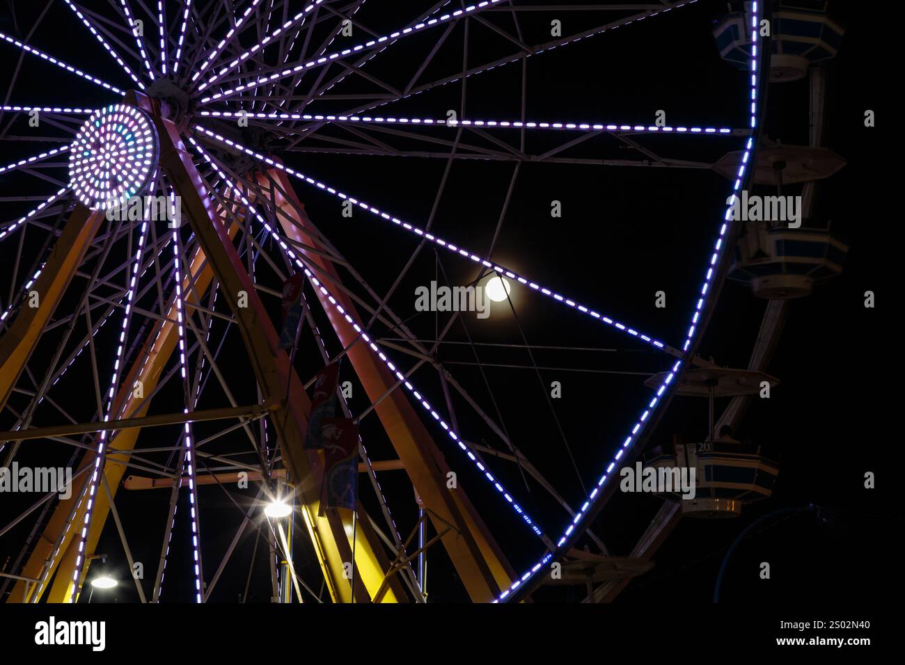 A large, illuminated Ferris wheel with a full moon in the background ...