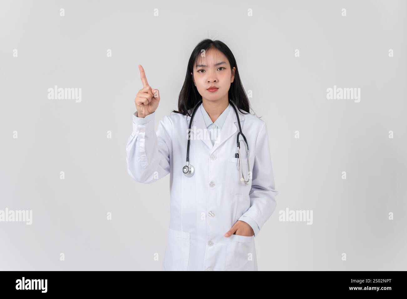 A serious, strict Asian female doctor in a white gown stands against a ...
