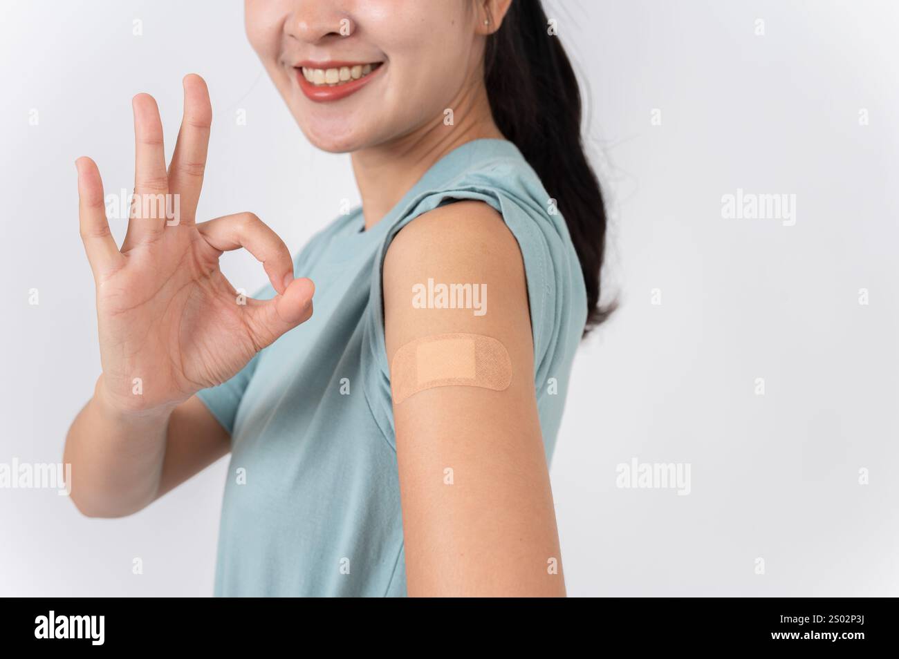 A smiling, carefree young Asian woman showing her arm with a plaster ...