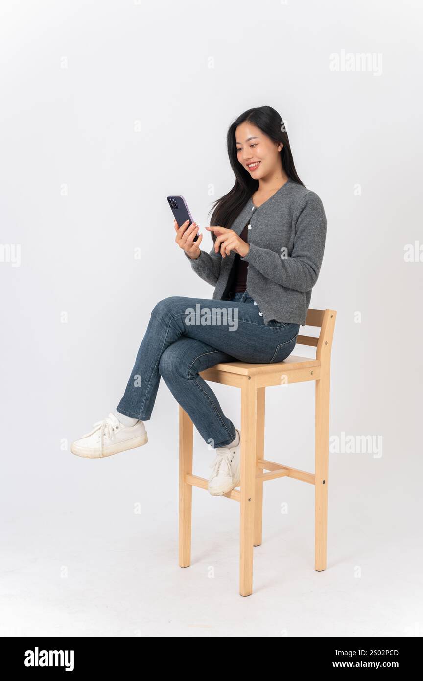An attractive Asian woman in casual clothes sits on a chair on a white ...