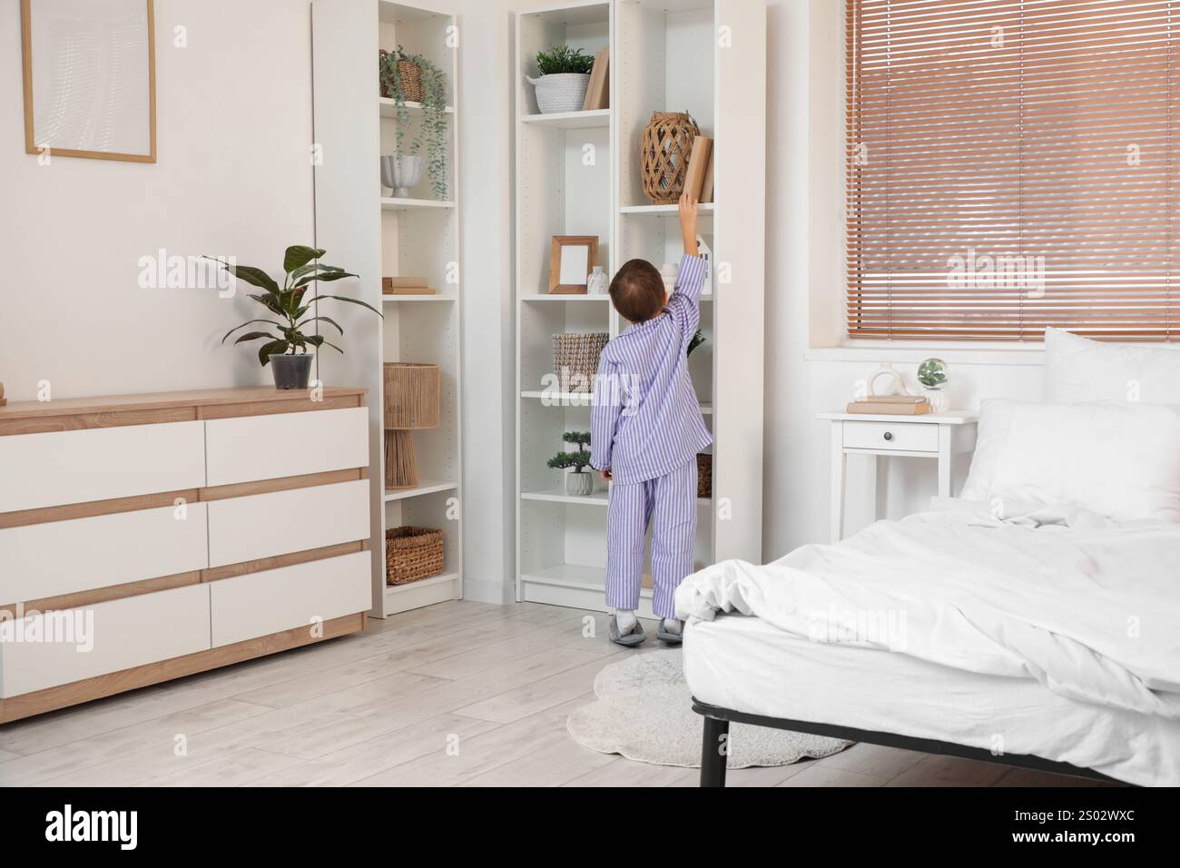 Cute little boy taking book from high shelf at home, back view. Child ...