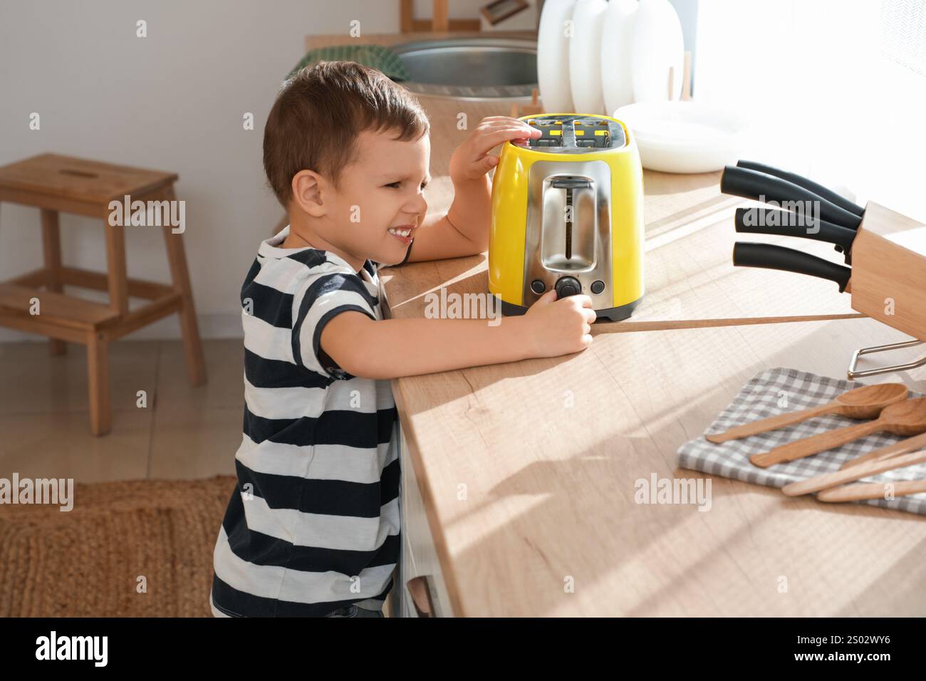 Cute little boy turning toaster on counter in kitchen. Child at risk ...