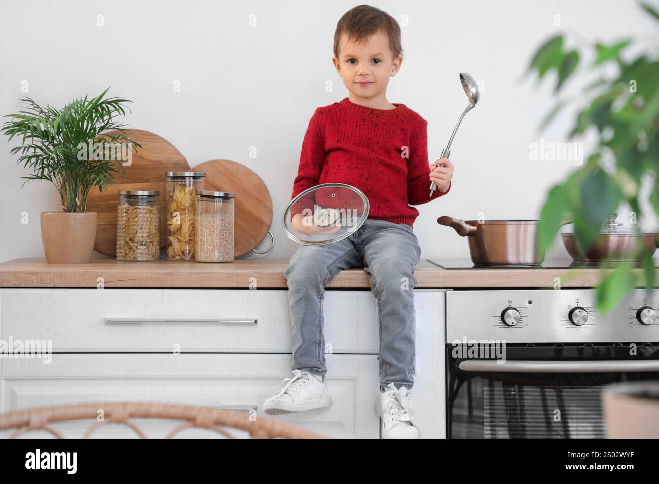 Cute little boy with ladle and lid sitting on counter in kitchen. Child ...