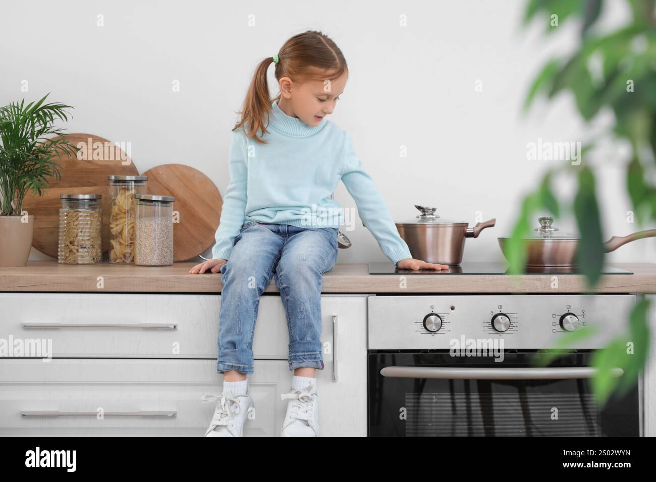 Cute little girl touching hot stove in kitchen. Child at risk Stock ...