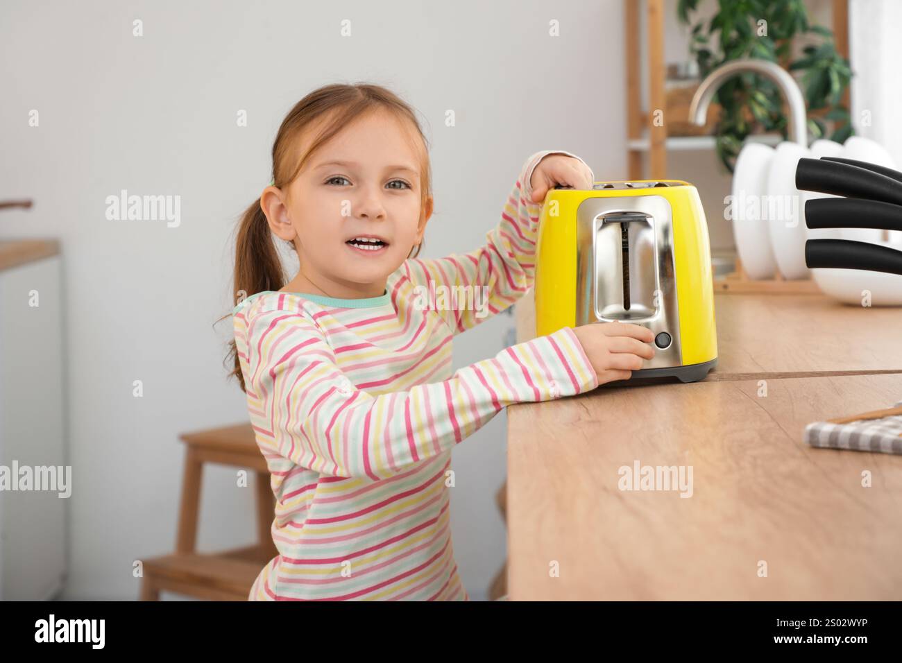 Cute little girl turning toaster on table in kitchen. Child at risk ...