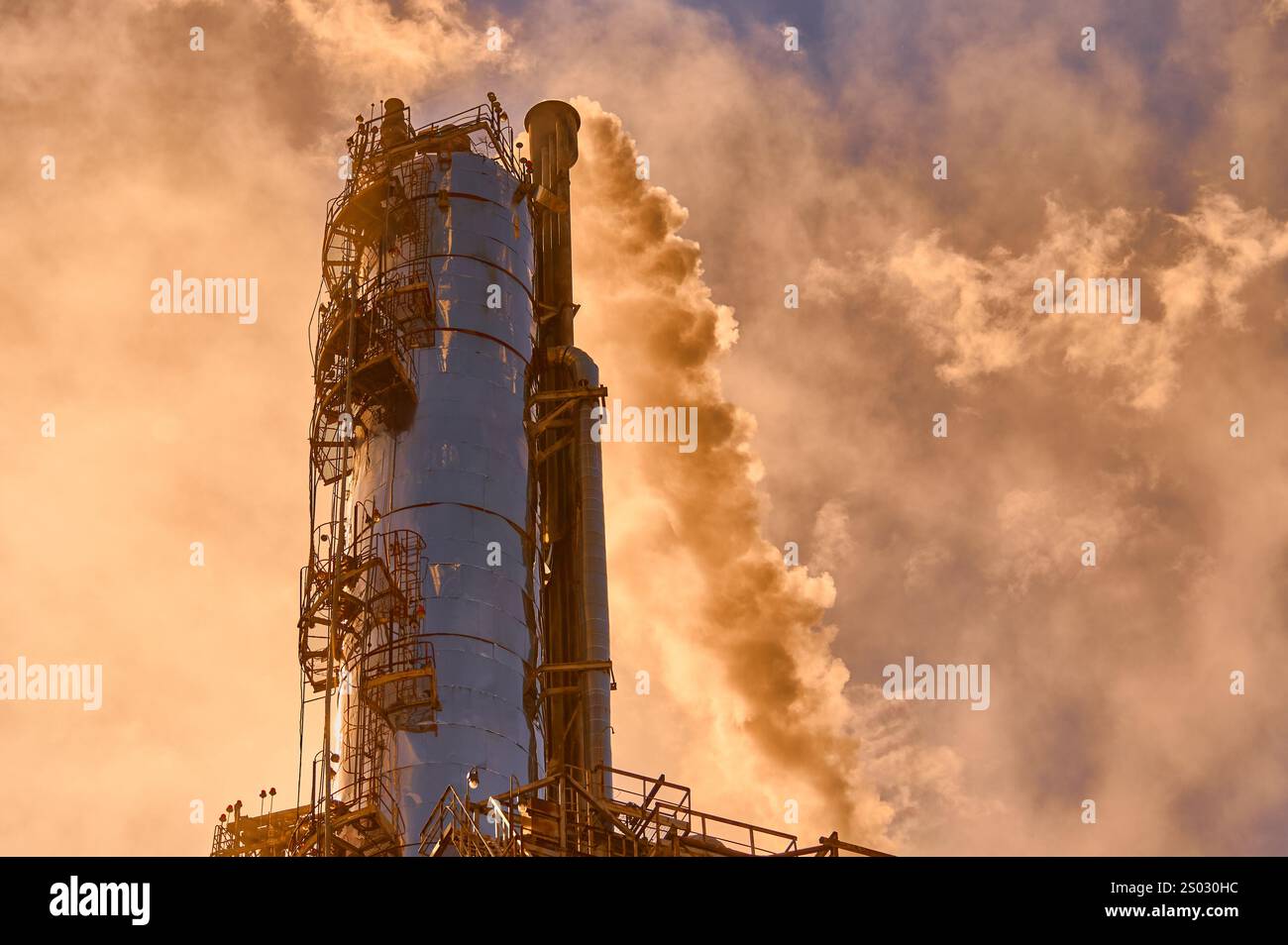 Sunset over a chemical plant with a focus on a distillation column ...