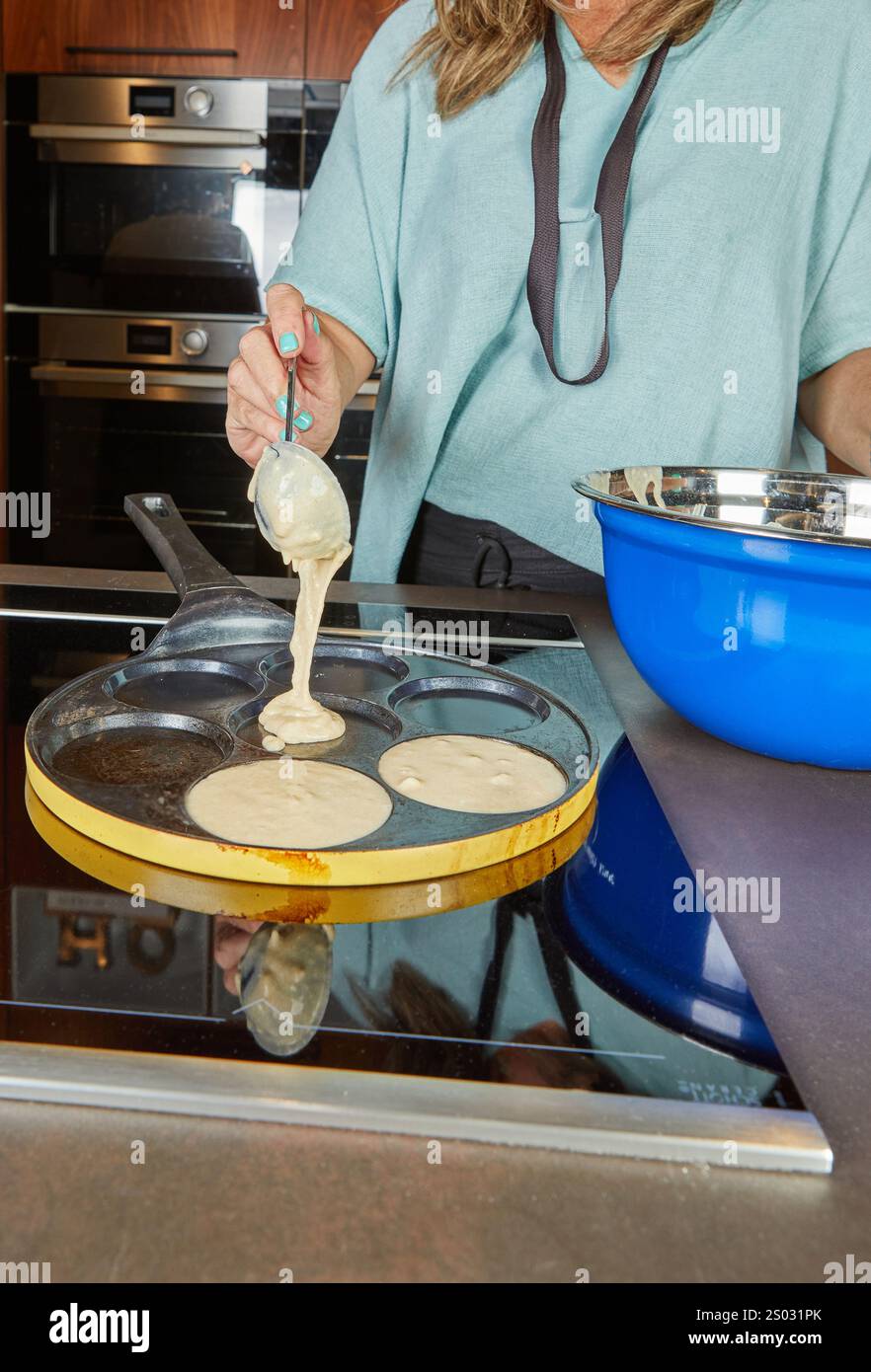 A person pours pancake batter into a round pancake mold on a stove ...