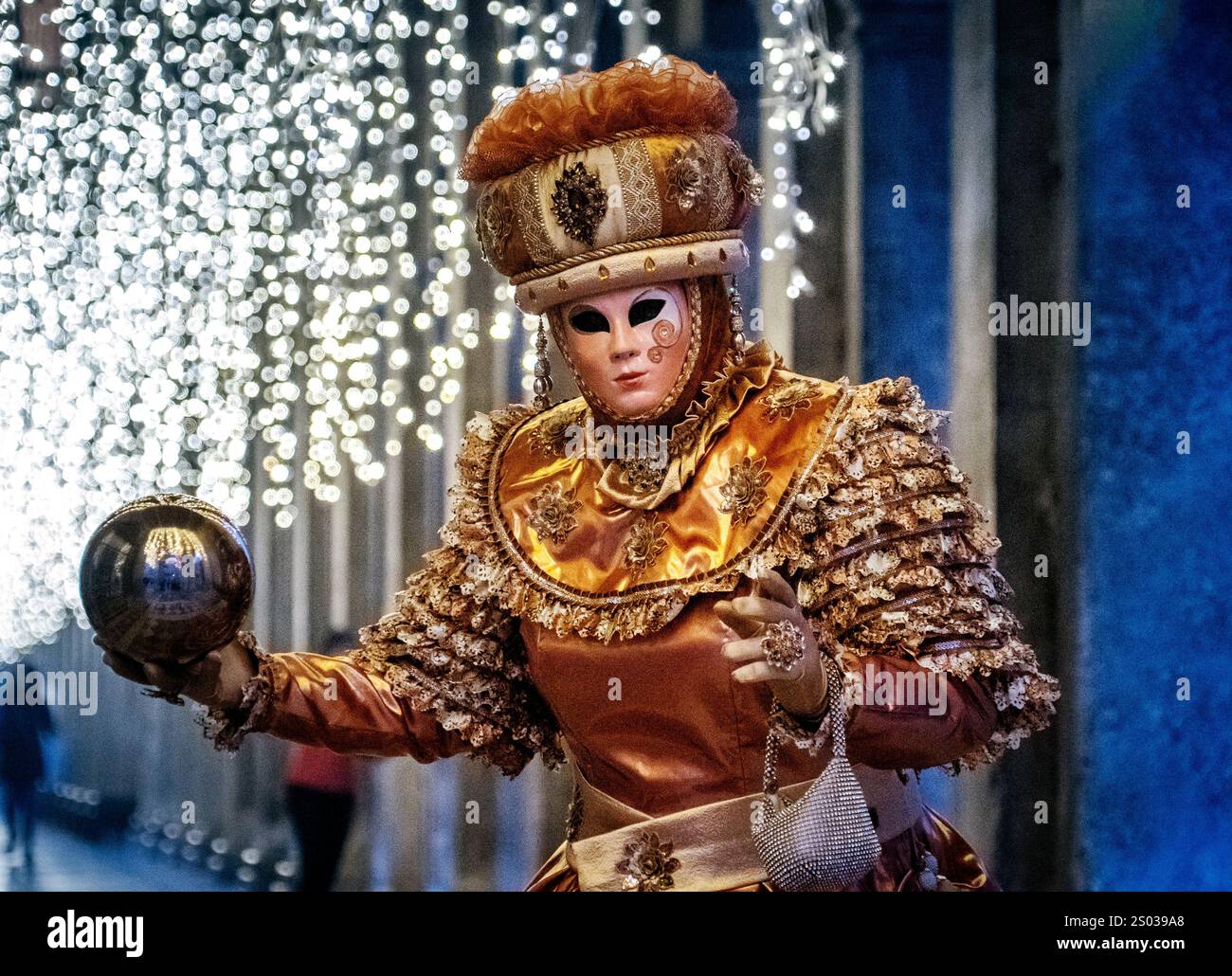 A person in an elaborate golden costume and mask, holding a reflective ...