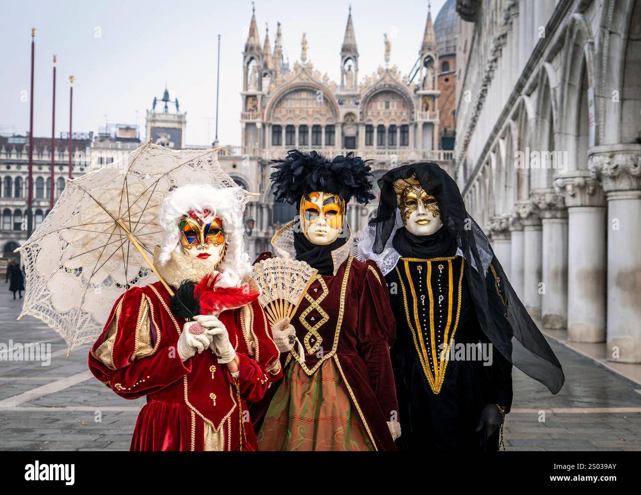 Three individuals in elaborate costumes and masks stand in a historic ...