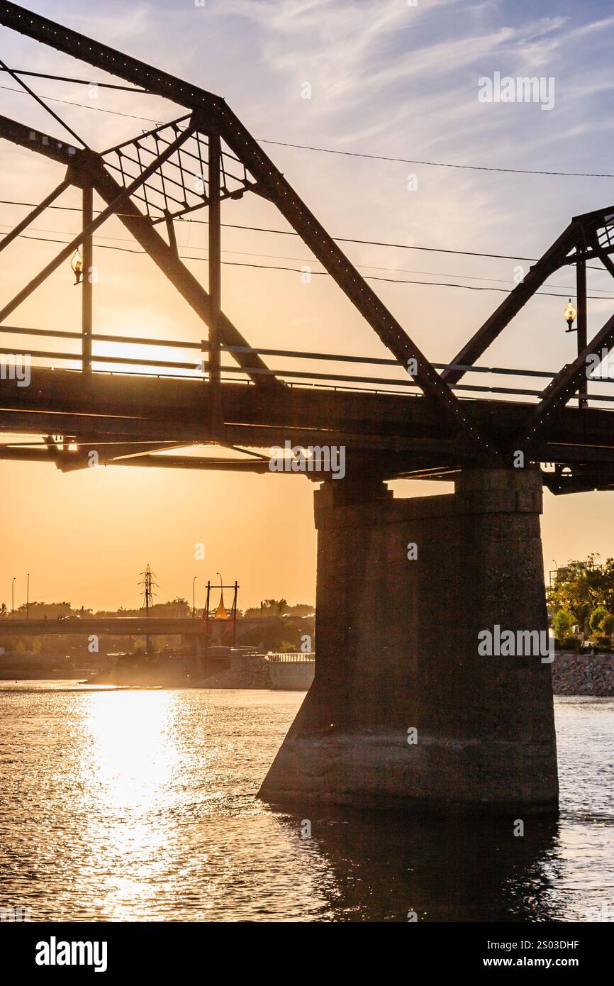 A bridge spans a river with a sunset in the background. The bridge is ...