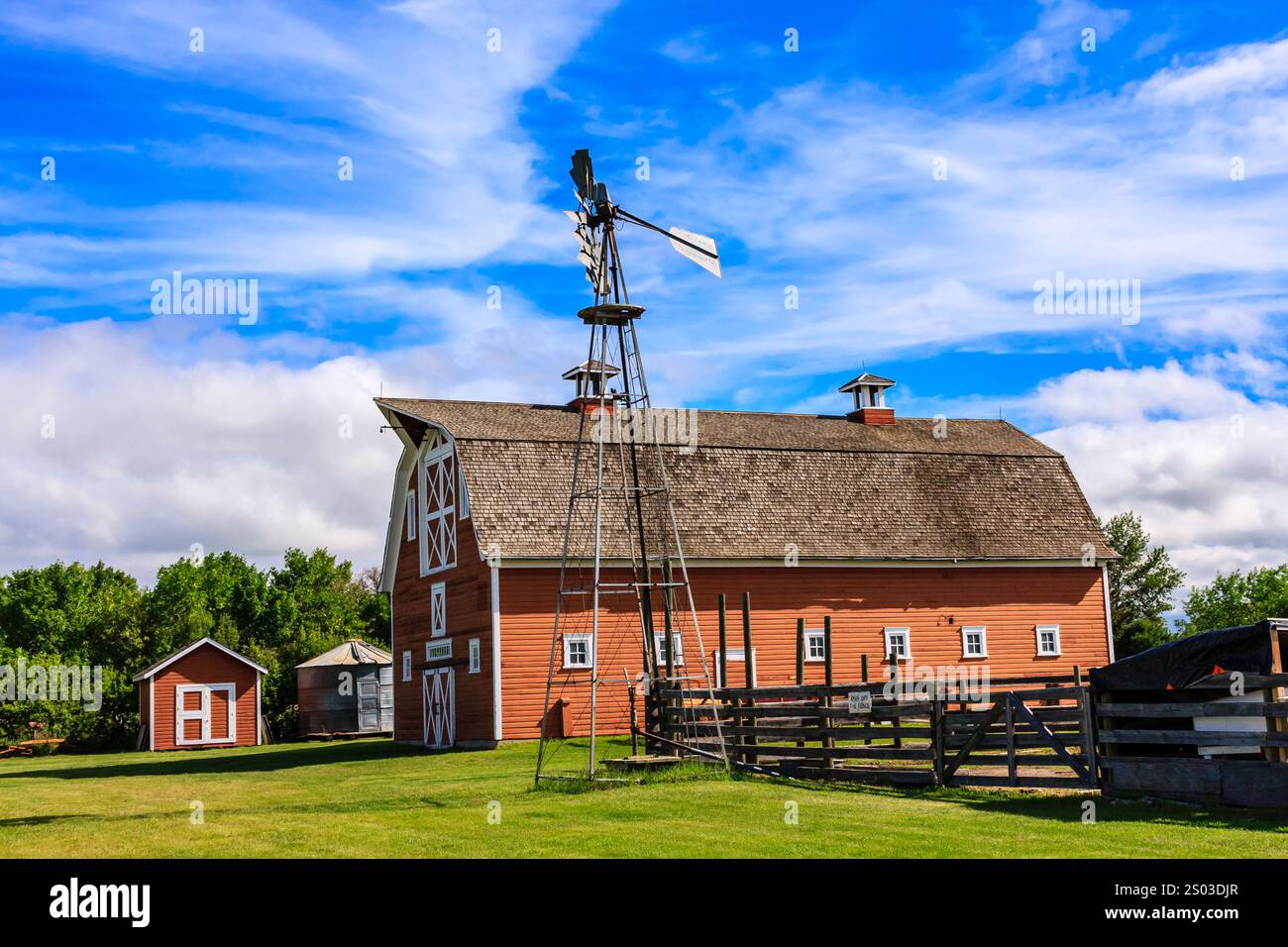 A windmill is on top of a red barn. The barn is surrounded by a fenced ...