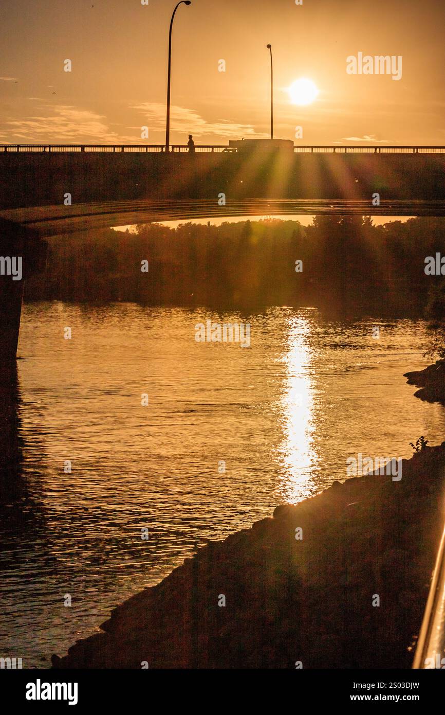 A bridge over a river with a sun setting in the background. The sun is ...