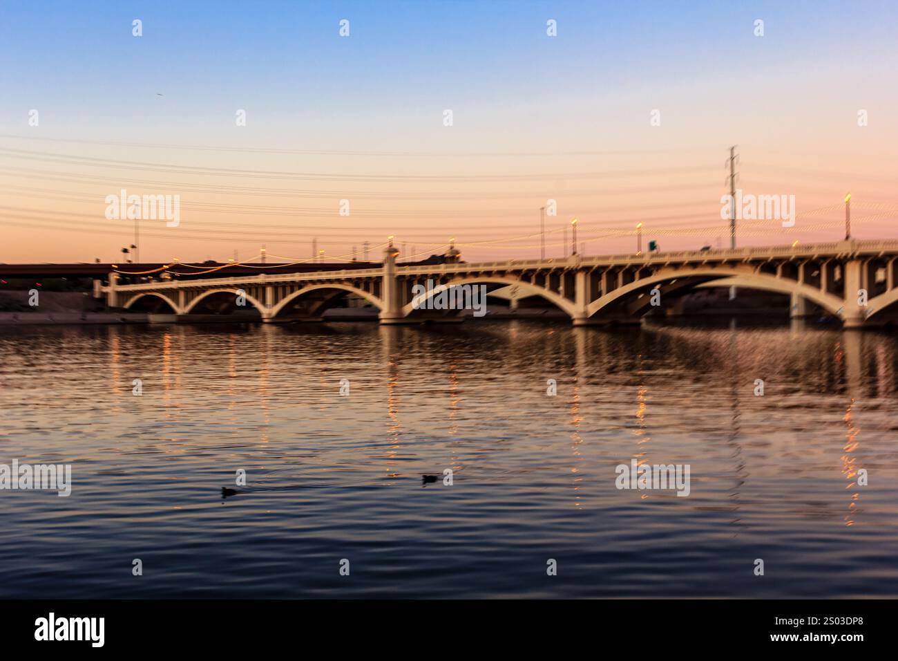 A bridge spans a river with a beautiful sunset in the background. The ...
