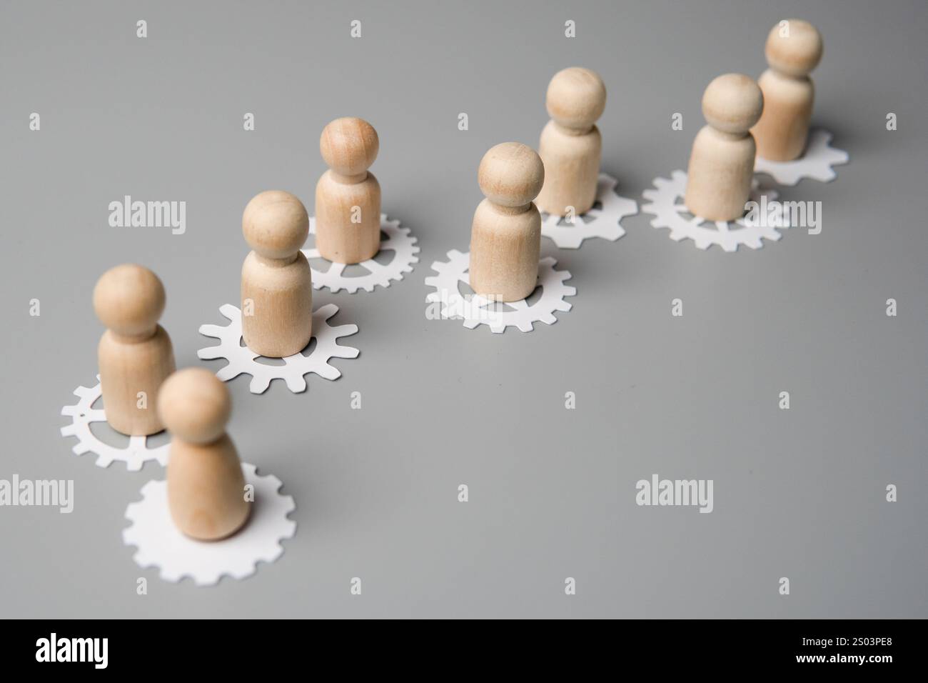 A conceptual image with wooden figures standing on interconnected gears ...