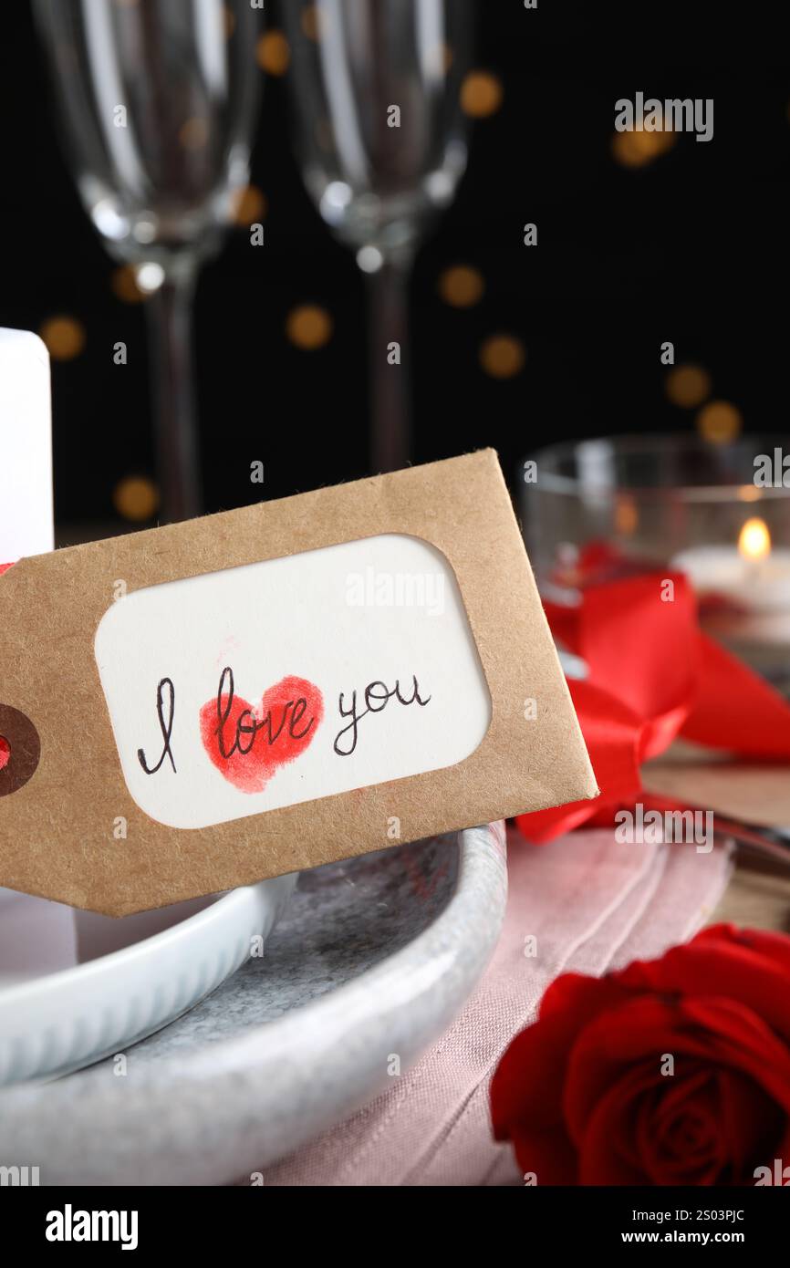 Beautiful place setting and tag with phrase I Love You on table against blurred lights, closeup ...