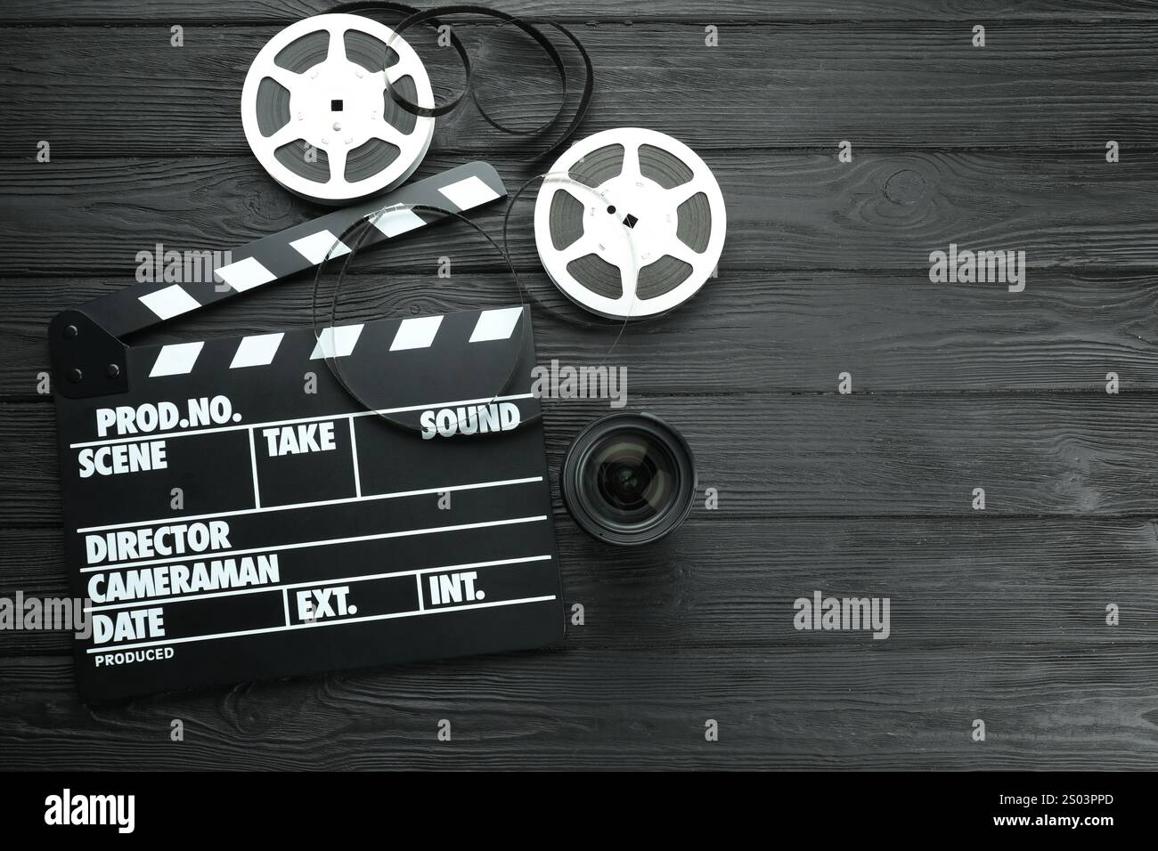 Movie clapper, film reels and camera lens on black wooden table, flat ...