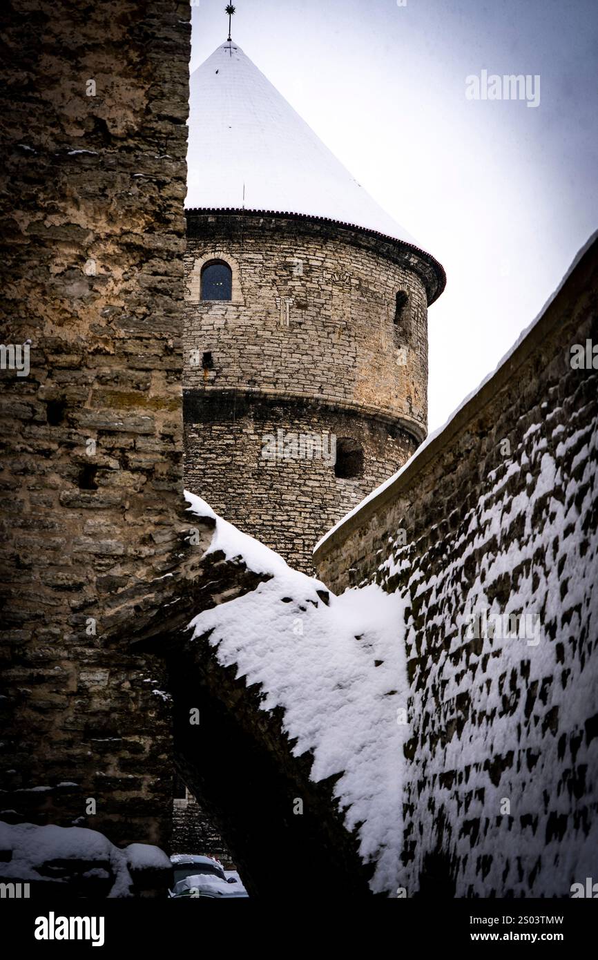 A snow-covered stone wall with a tower in the background. The tower has ...