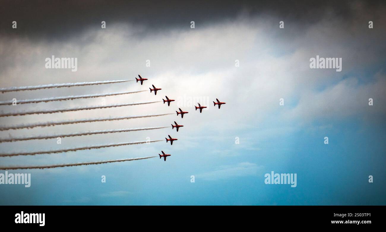 A formation of nine red aircraft performing an aerial display against a ...