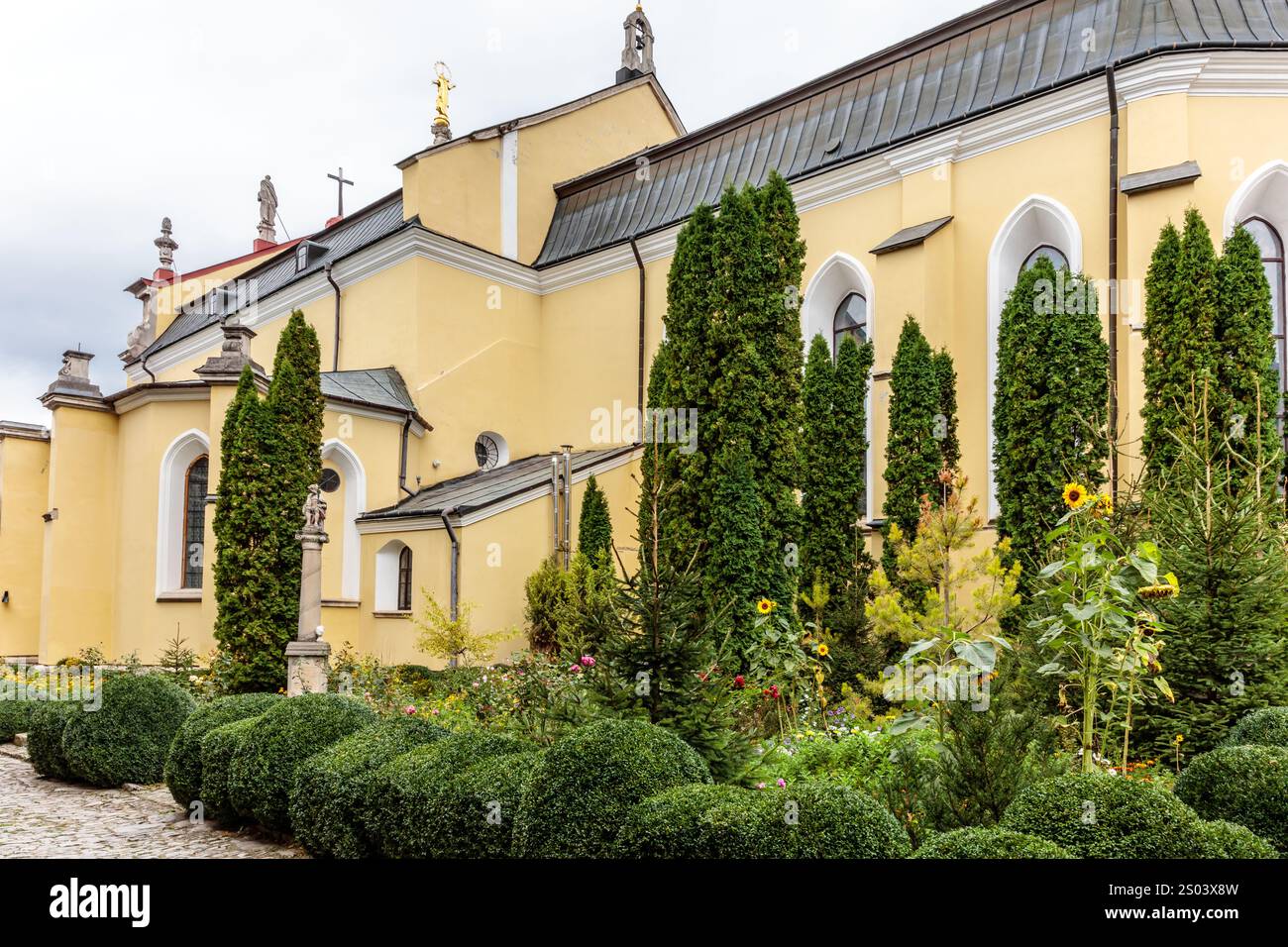 A large yellow building with a green roof and a green hedge. The ...