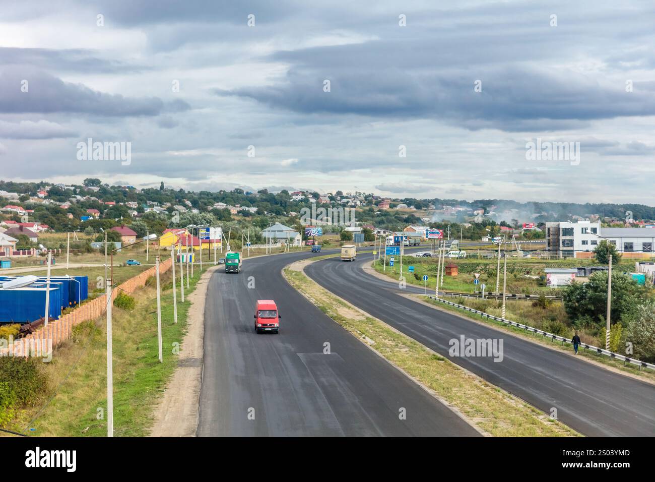 A road with a few cars and trucks on it. The road is surrounded by ...