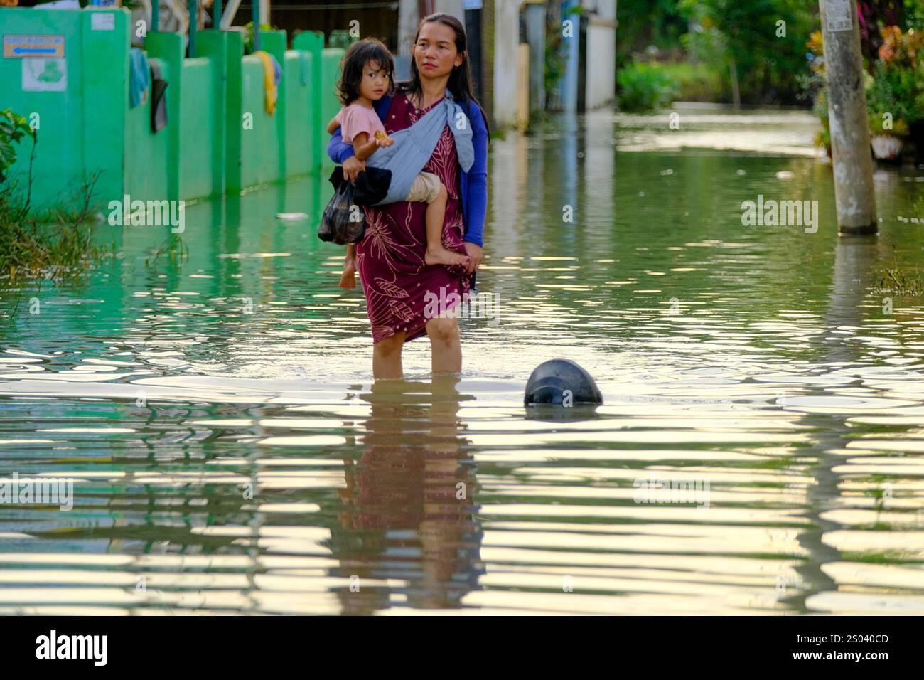 Makassar, Indonesia. 24th Dec, 2024. A woman holding a girl walks through flood water after ...