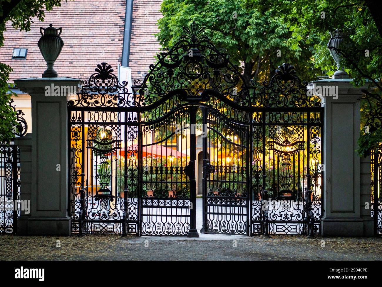 A beautifully ornate wrought iron gate partially open, revealing a glimpse of a vibrant garden ...