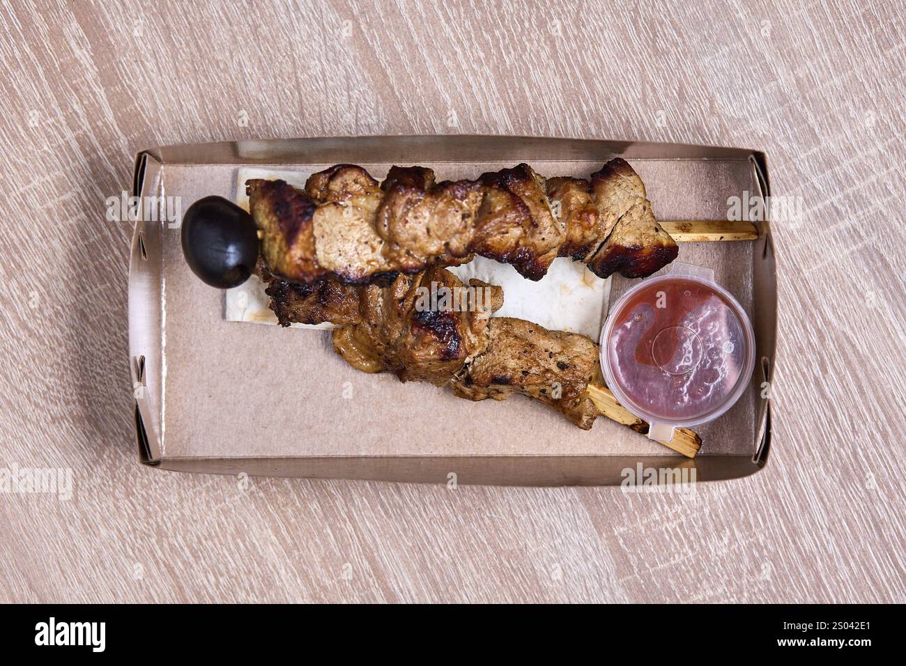 Two skewers of grilled chicken with sauce and an olive in a cardboard ...