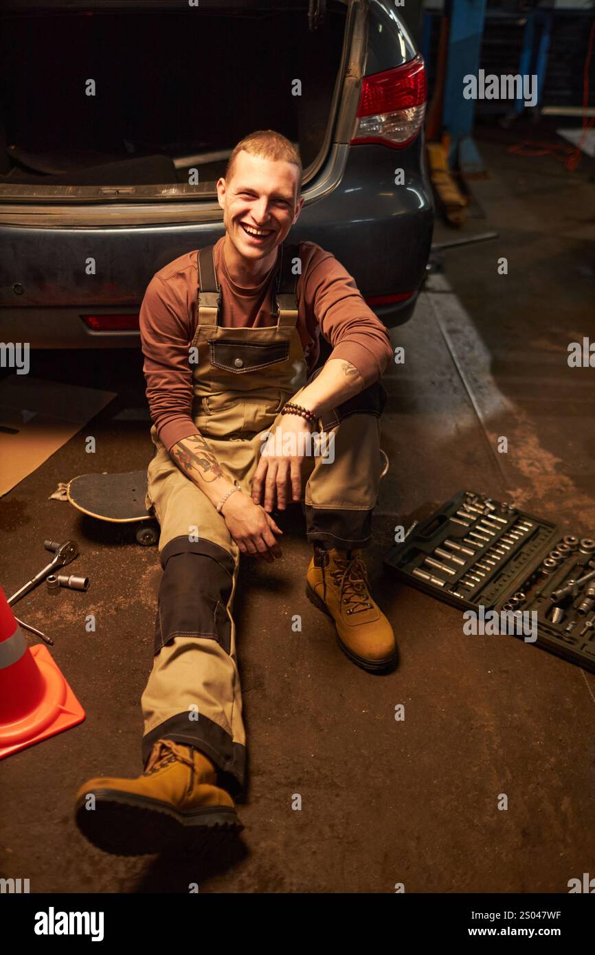 Portrait of happy mechanic sitting on the floor and laughing while ...
