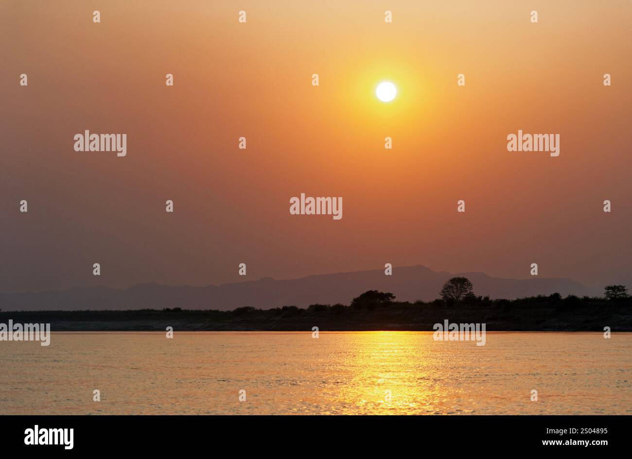 Serene view of a golden sunset over a calm river with distant hills ...