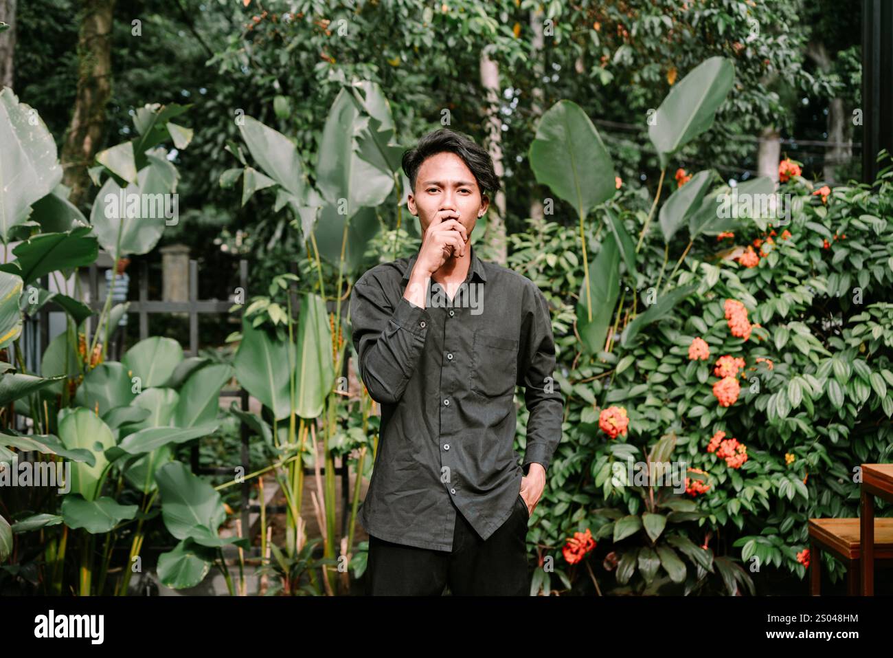 A Southeast Asian man striking a pose, holding his mouth with one hand ...
