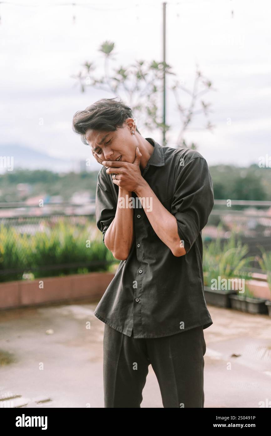 Southeast Asian man holding his cheek with a pained expression, showing ...