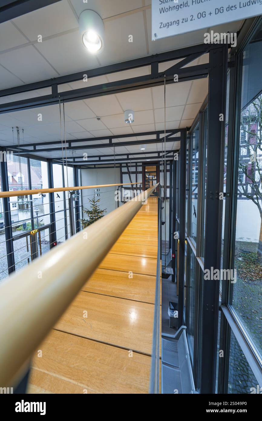 Light-flooded passageway with wooden railings and large glass windows ...