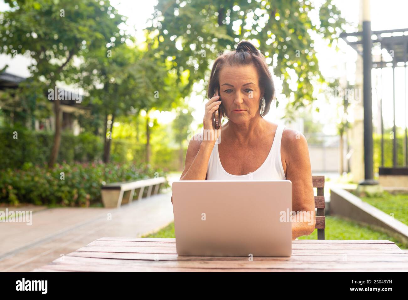 Mature beautiful woman sitting and using laptop computer outdoors ...