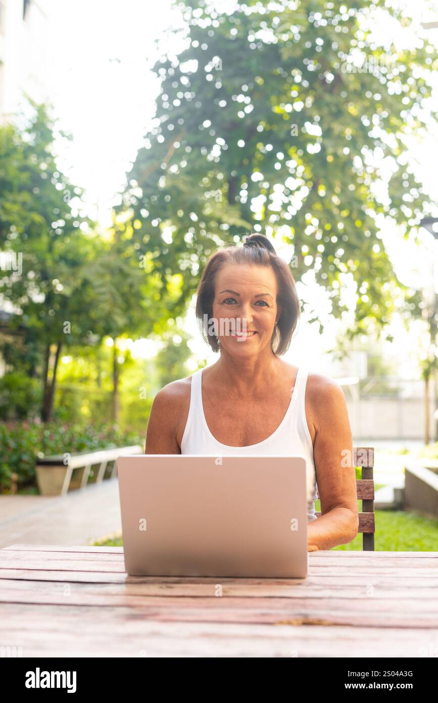 Mature beautiful woman sitting and using laptop computer outdoors ...