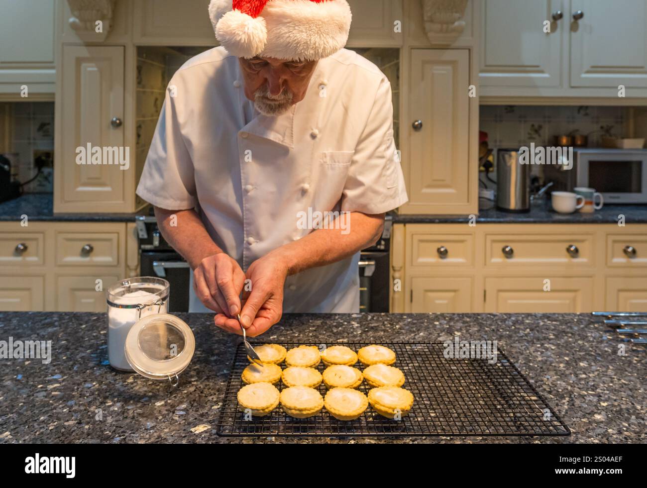 Senior man wearing chef whites and Santa hat sprinkling sugar making ...