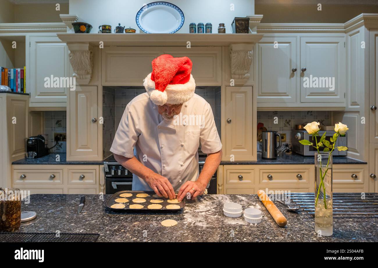 Senior man wearing chef whites and Santa hat filling pastry cases with ...