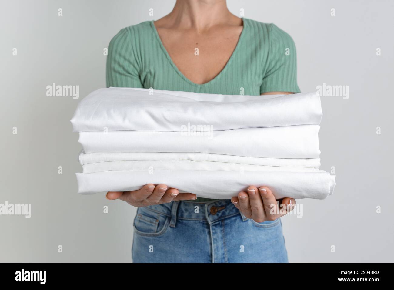 Woman holding stack of clean bed linens on light grey background Stock ...